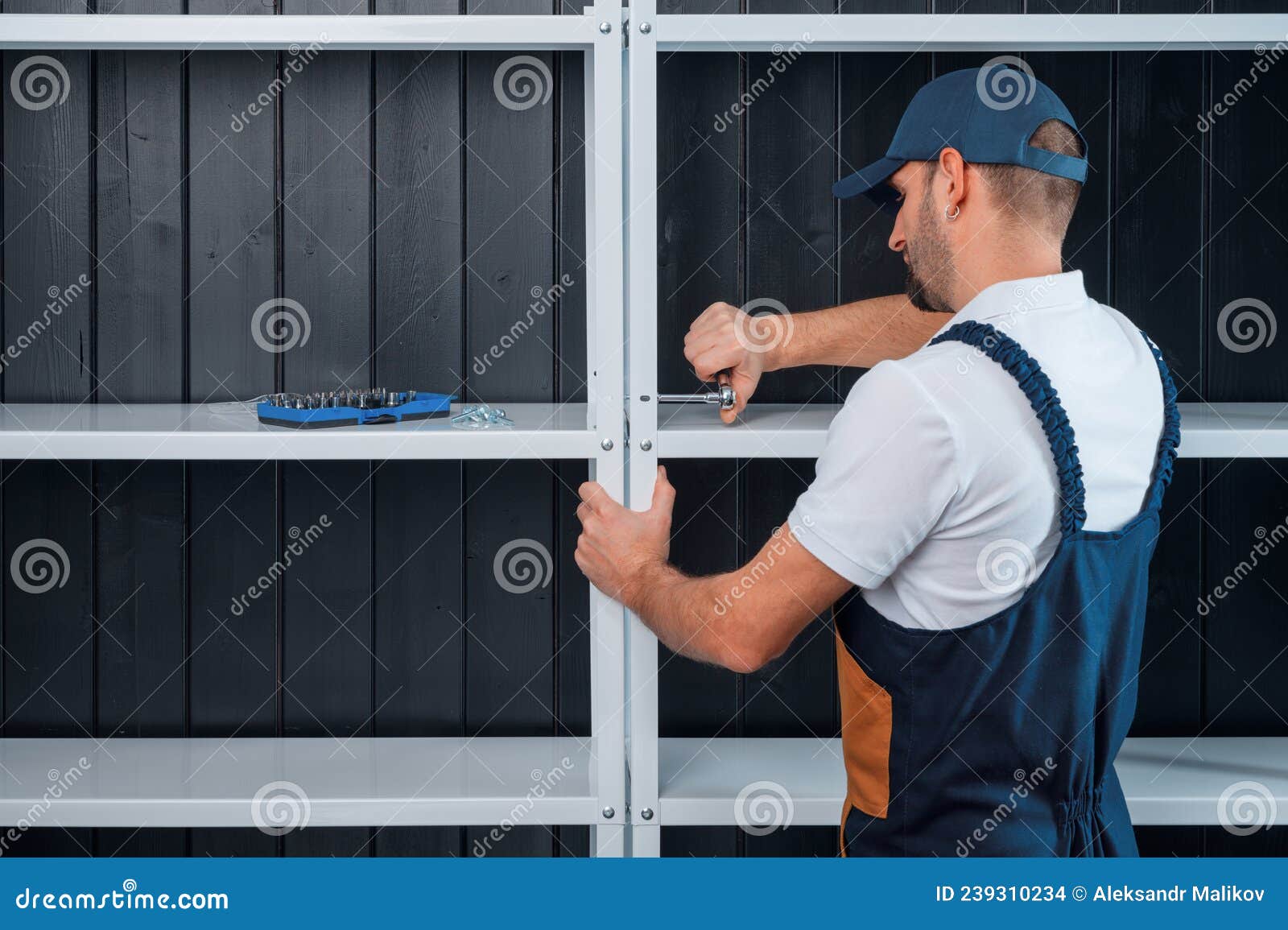 A Uniformed Worker is Assembling a White Metal Shelving Against a Black ...