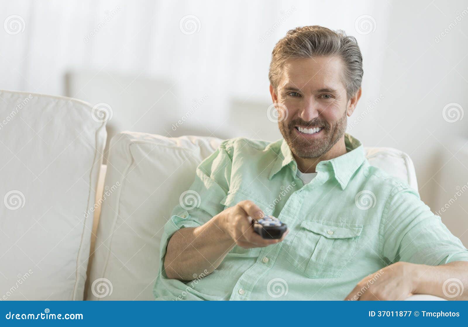 Uomo Che Si Siede Su Sofa with Remote Control Immagine Stock - Immagine ...