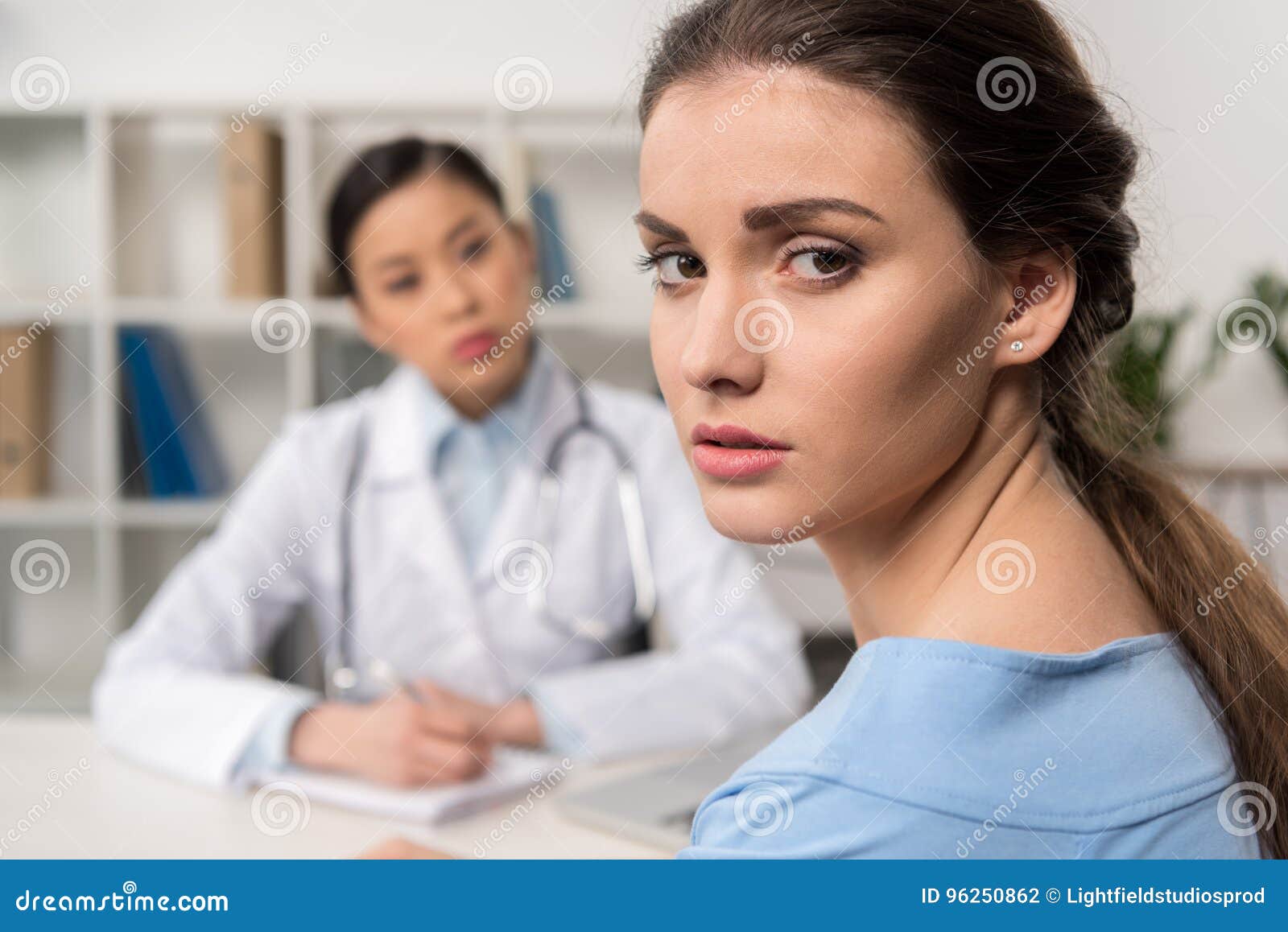 Upset Patient Looking at Camera with Doctor Sitting at Workplace Behind ...
