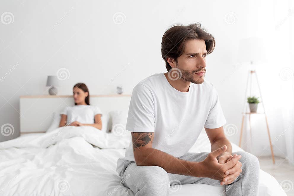 Upset Sad Offended Millennial European Husband And Wife Sitting On Bed