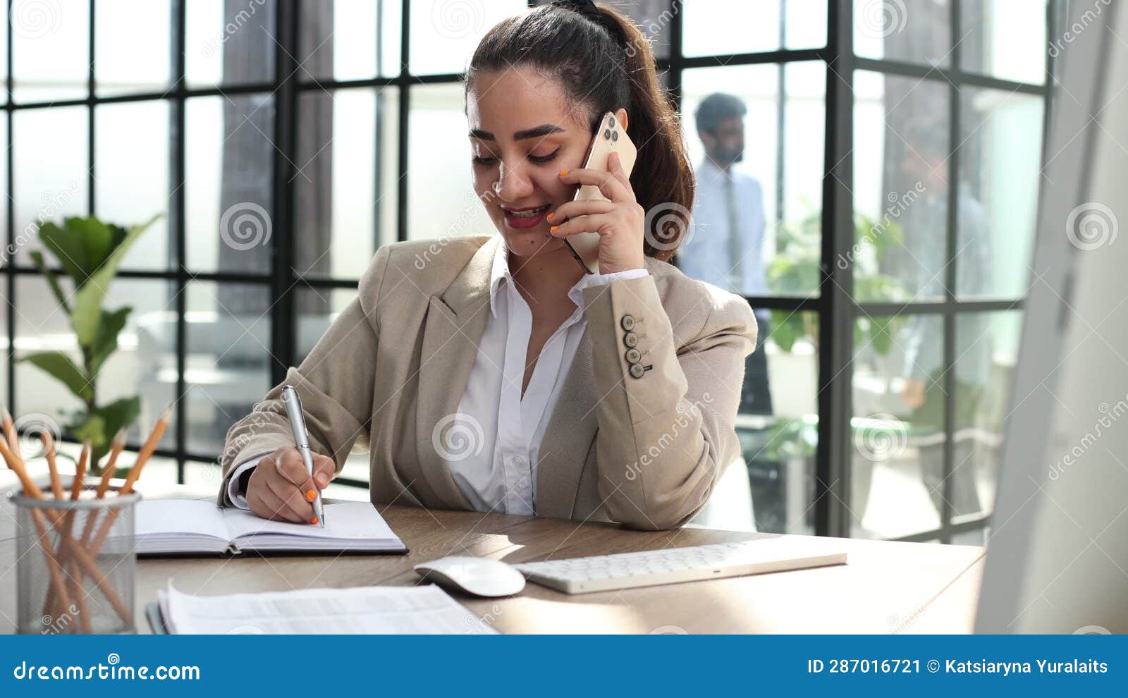 Charming Woman Using Her Mobile Phone while Writing on a Sheet of Paper ...