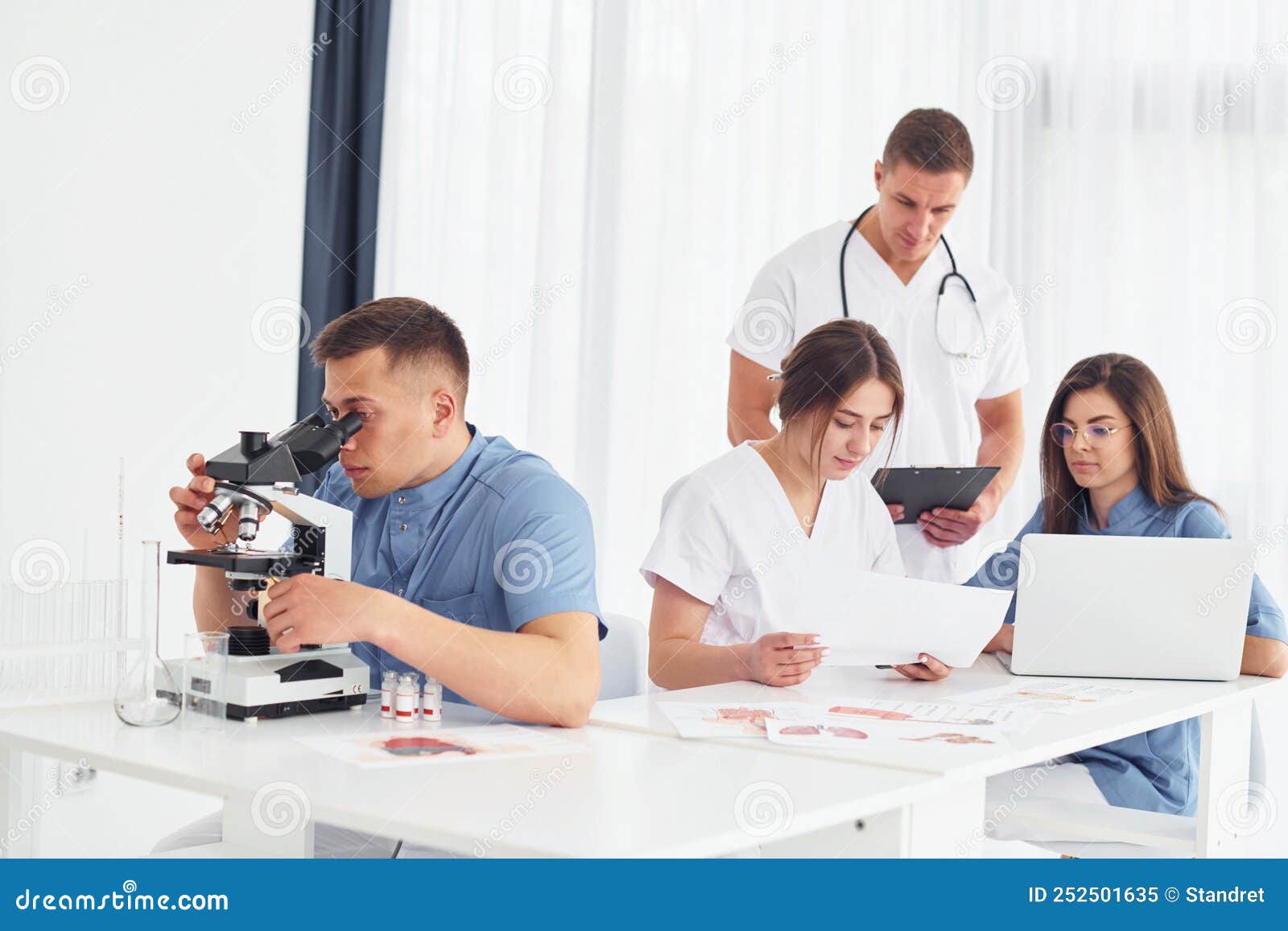 Using Microscope. Group of Young Doctors is Working Together in the ...