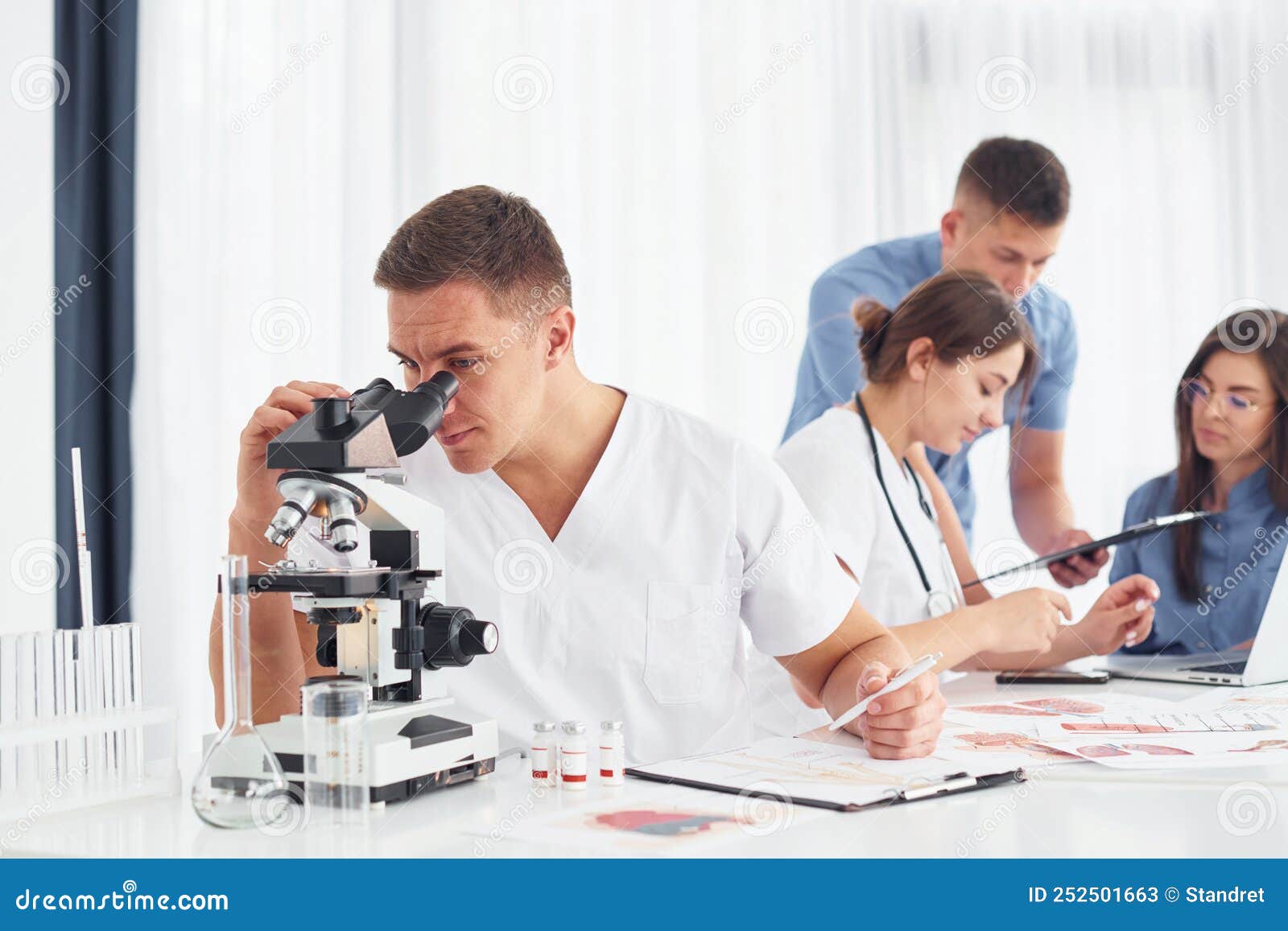 Using Microscope. Group of Young Doctors is Working Together in the ...