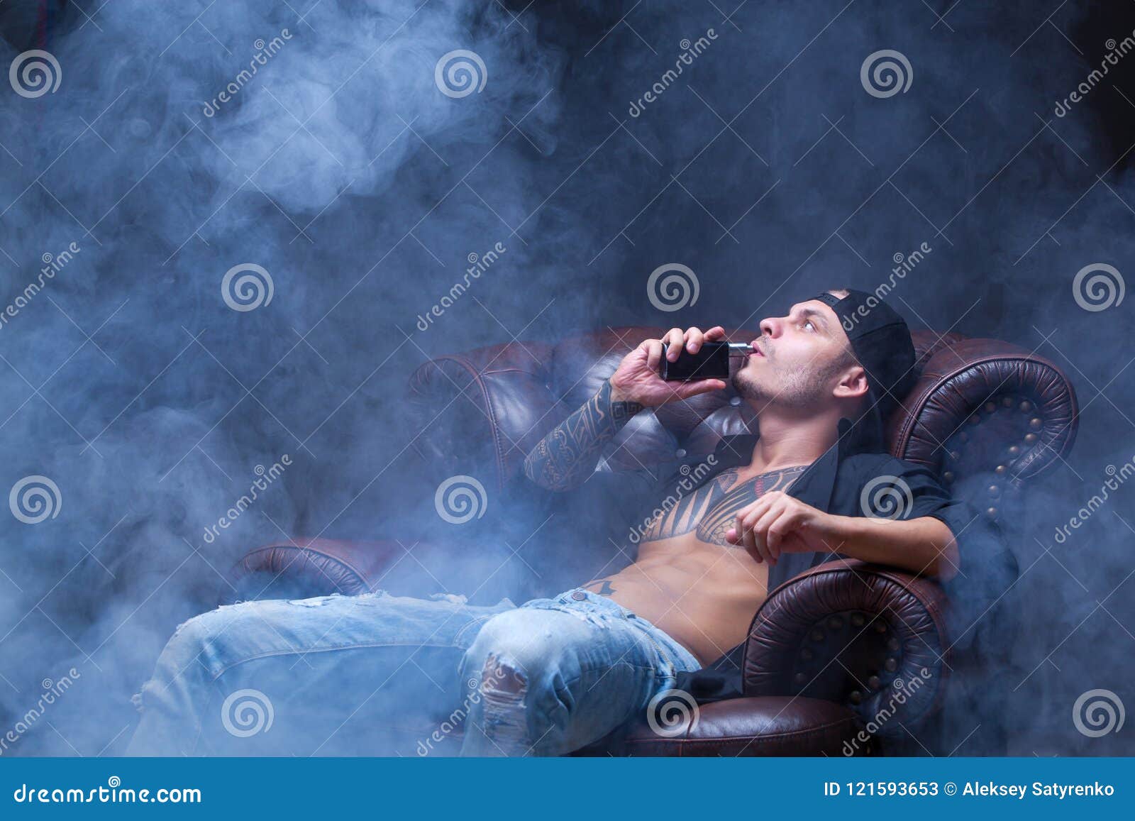 Vaper. the Man with Tattoos Sits on a Leather Sofa Smoke an Electronic ...