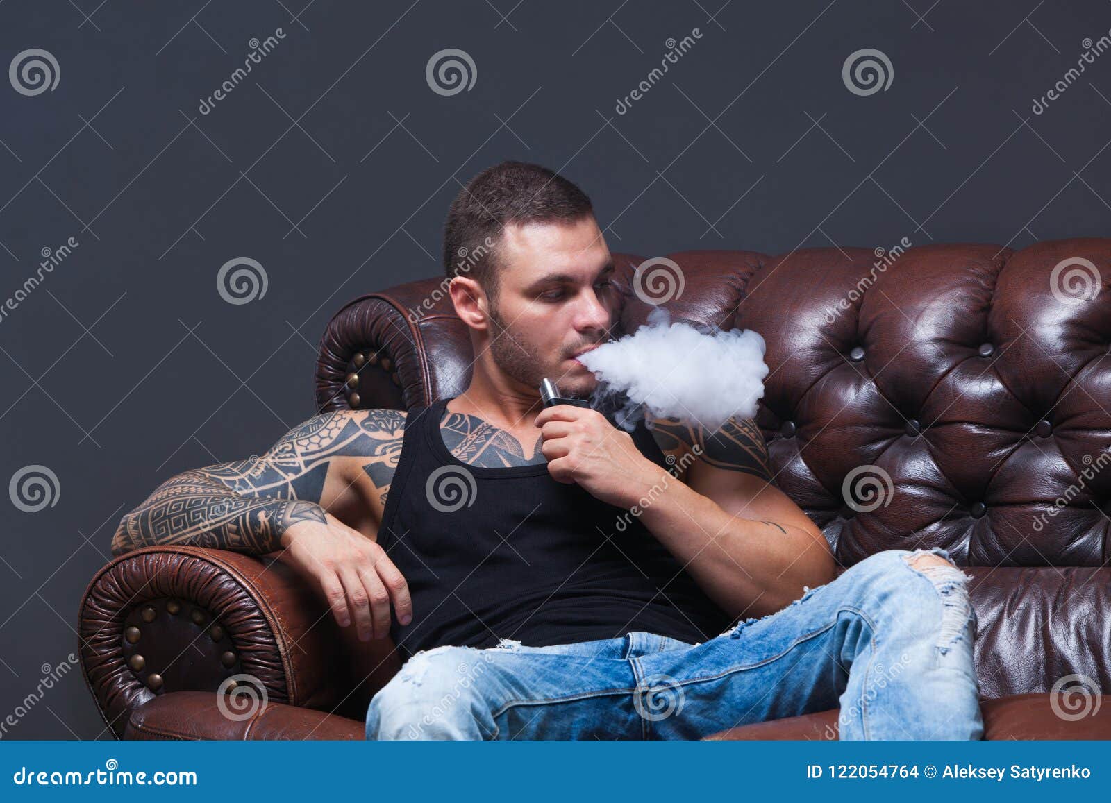 Vaper. the Man with Tattoos Sits on a Leather Sofa Smoke an Electronic ...