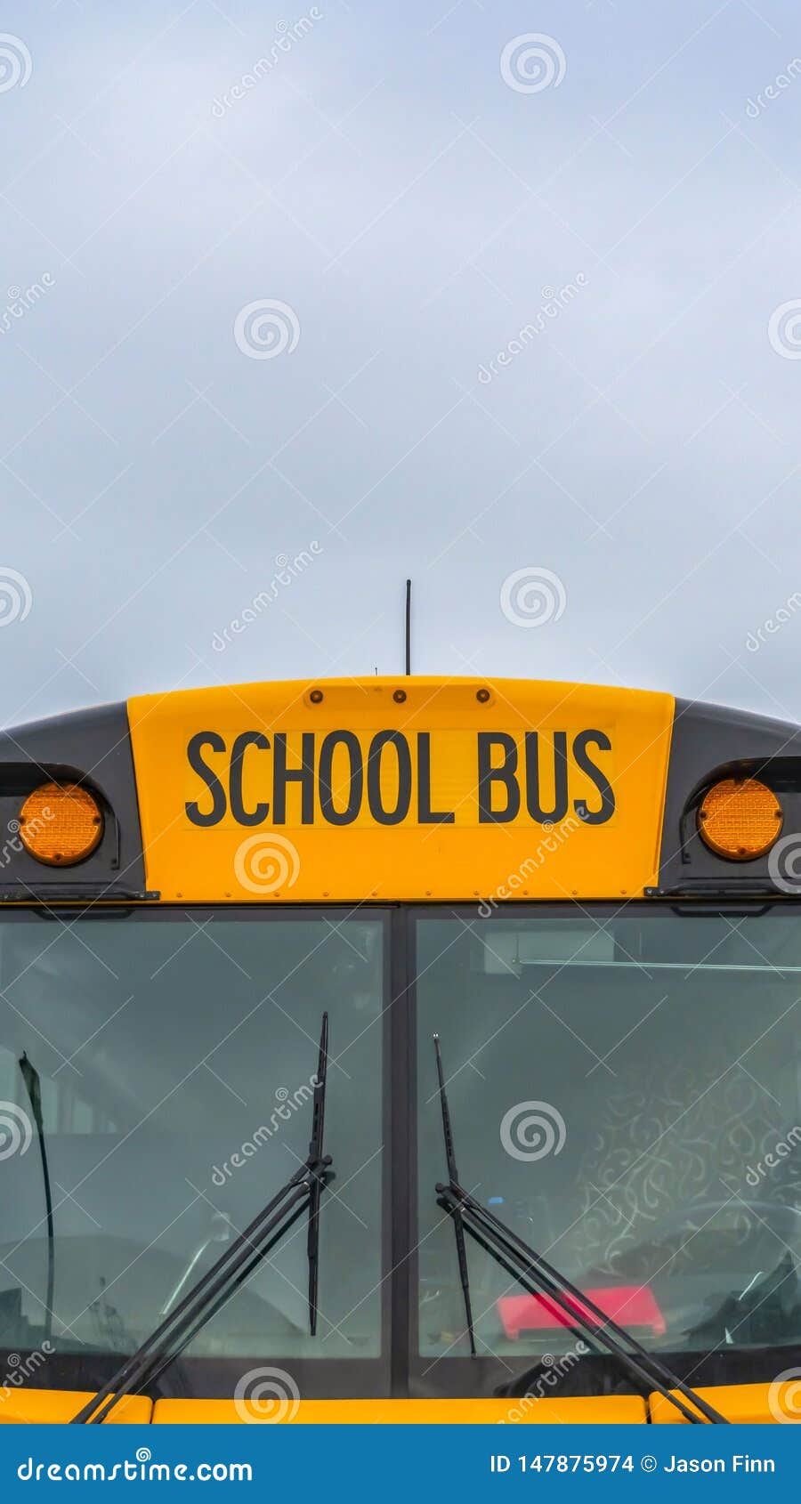 Vertical Front View of a Yellow School Bus with Homes and Cloudy Sky in ...