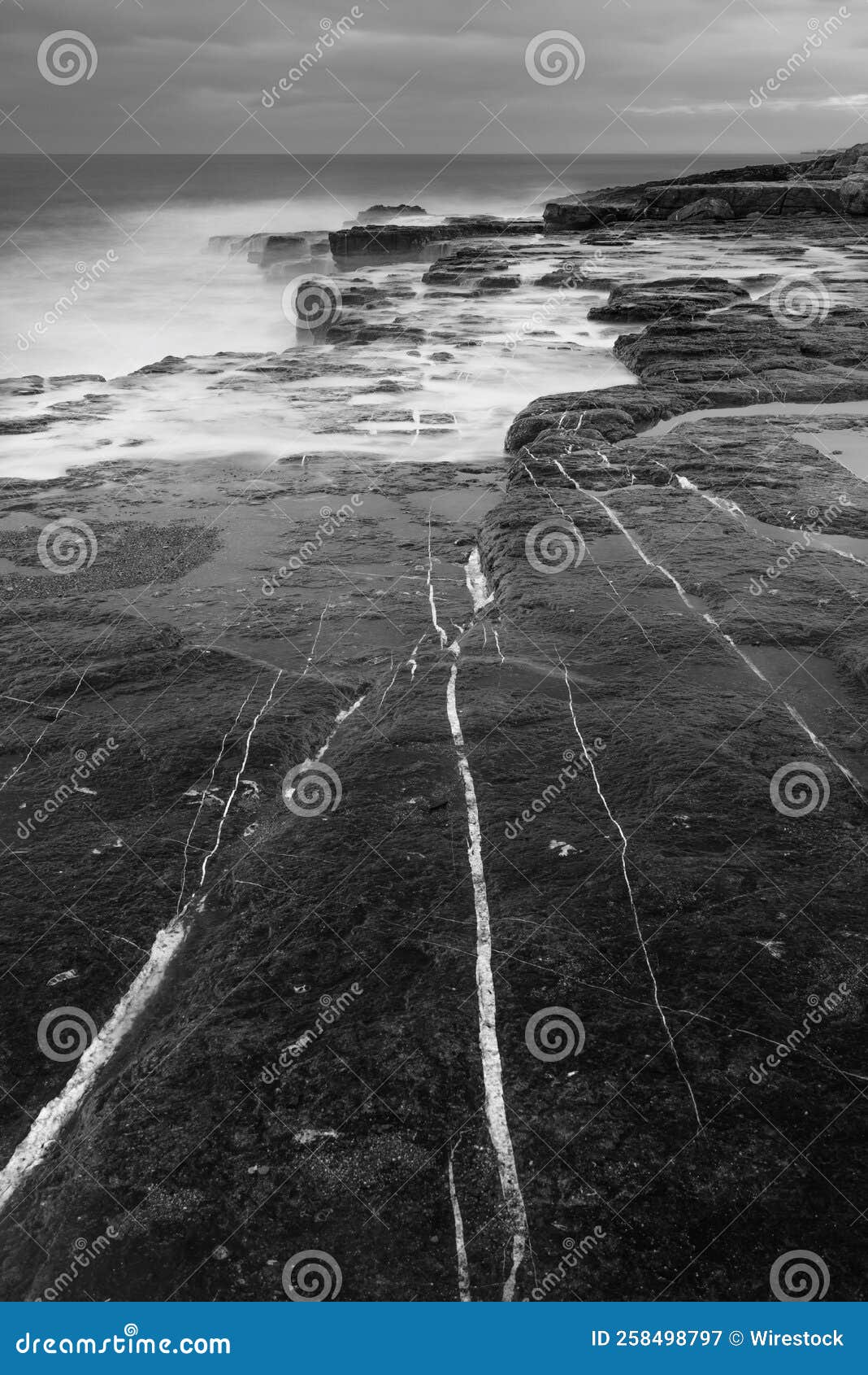 Vertical Grayscale of Waves Washing the Sandy Beach with Rocky Cliffs ...