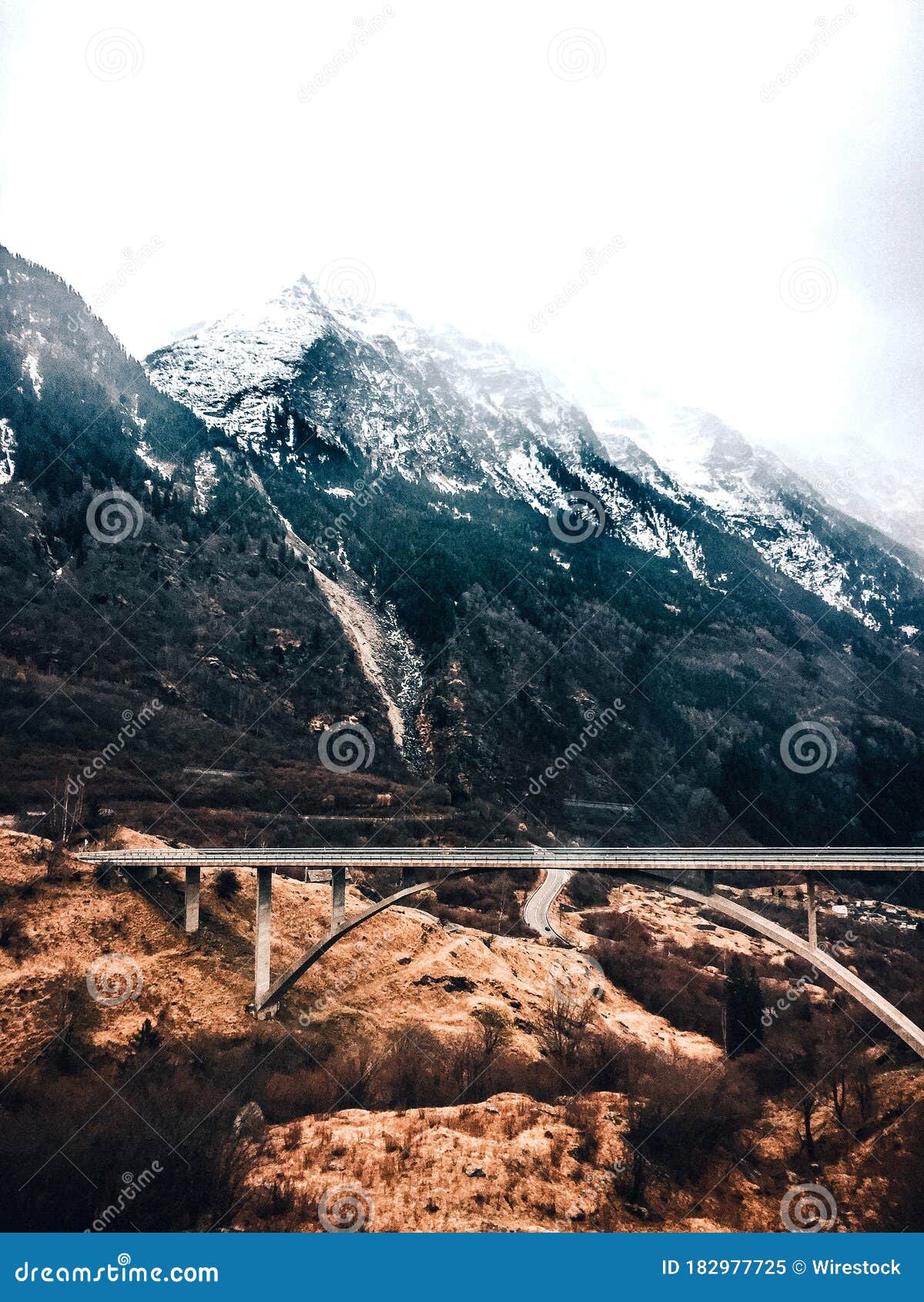 Vertical Shot of a Bridge Over Hills with Mountains Covered in Snow on ...