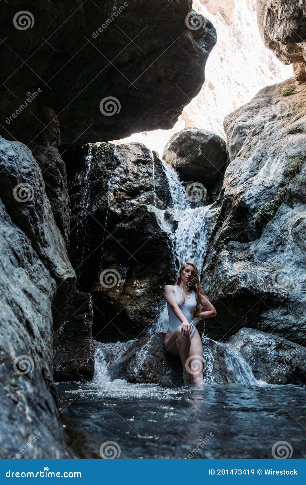 Vertical Shot Of A Woman In A Wet One Piece Swimsuit Posing On A Rock