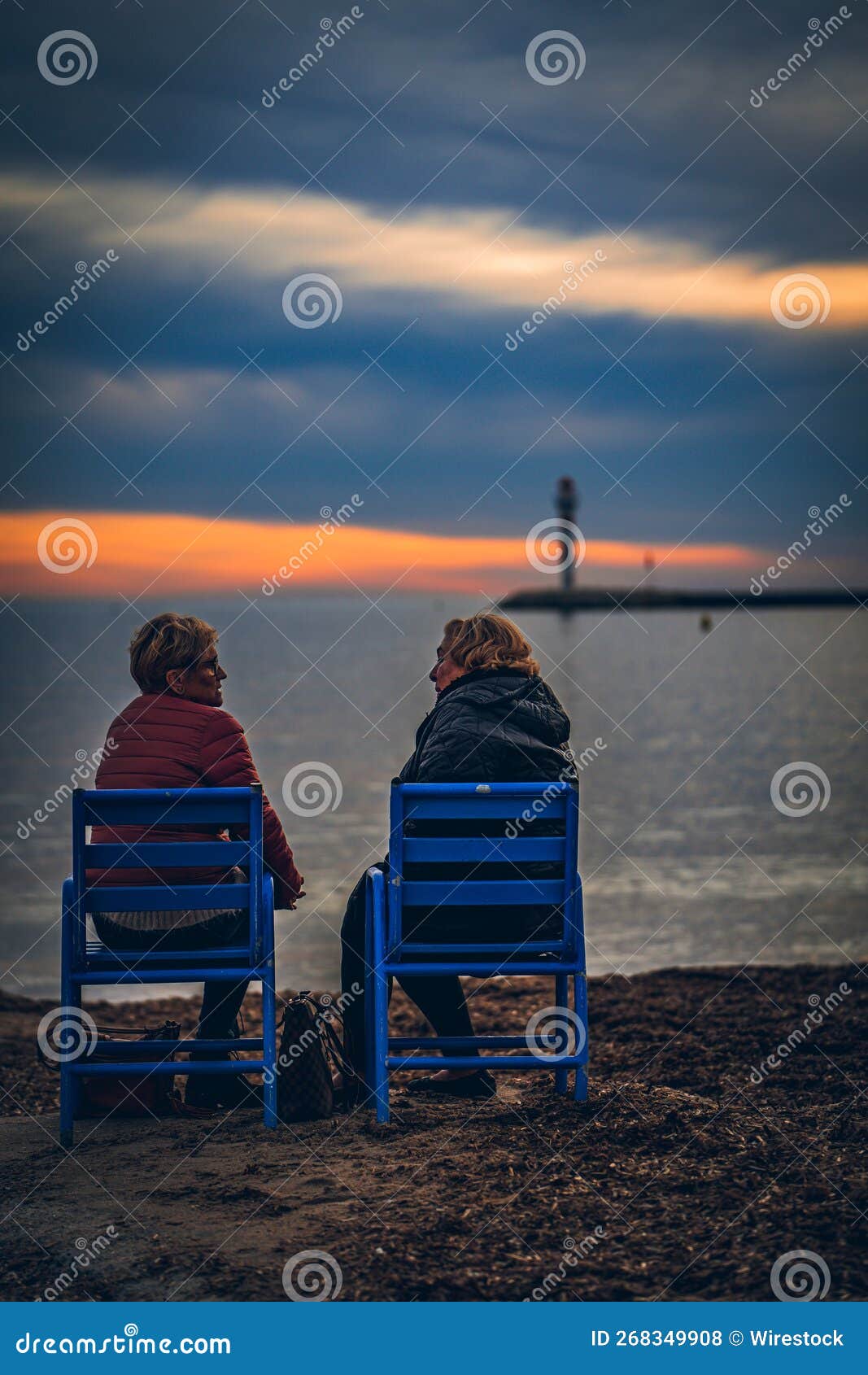 Vertical Shot Of Two Old Ladies Enjoying The Sunset At The Beach