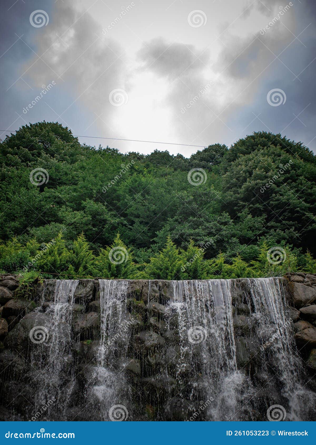 Vertical Shot of a Waterfall with Greenery and Cloudy Sky Over it Stock ...