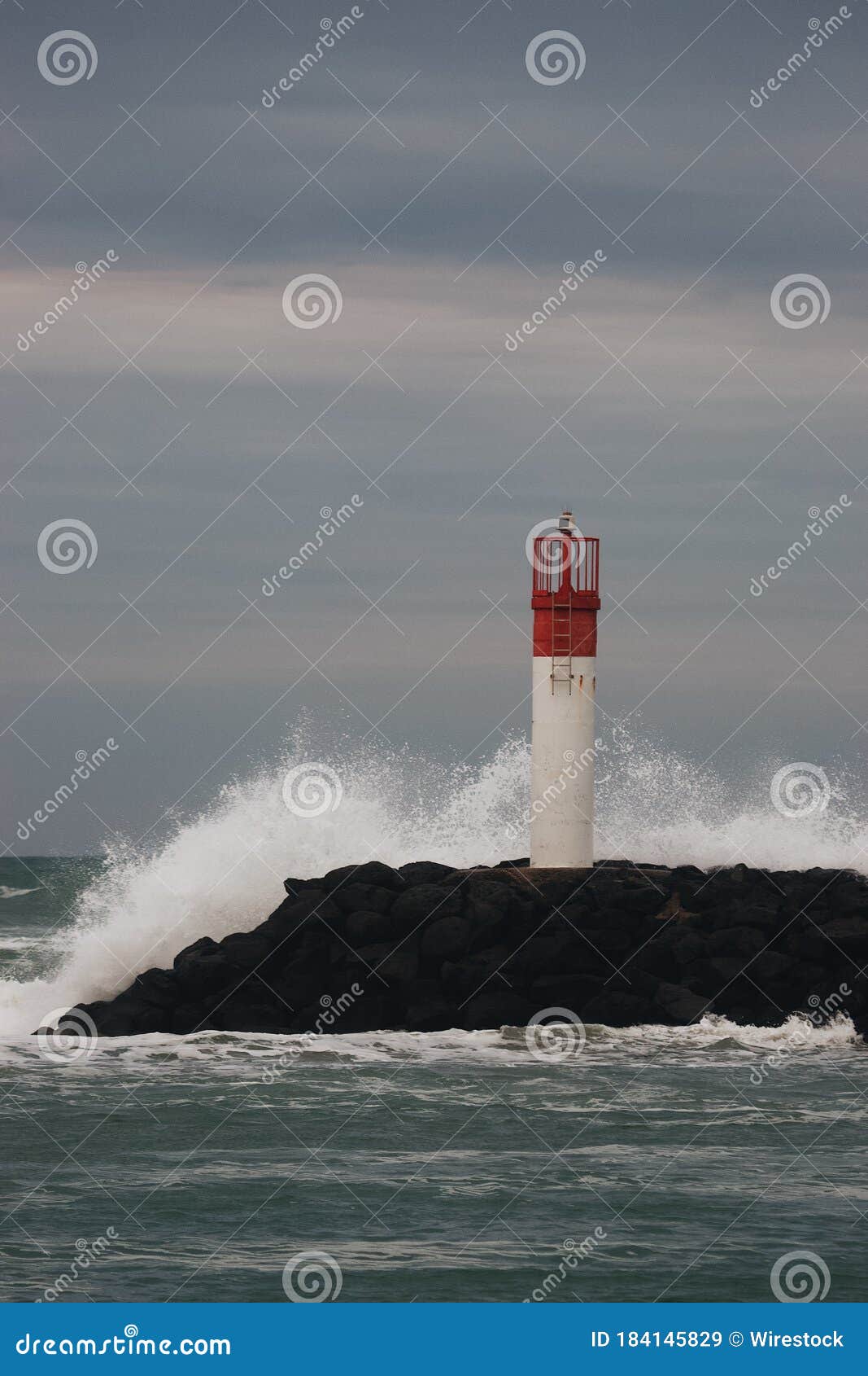 Vertical Shot a White Lighthouse with a Red Top and a Wave Hitting it ...
