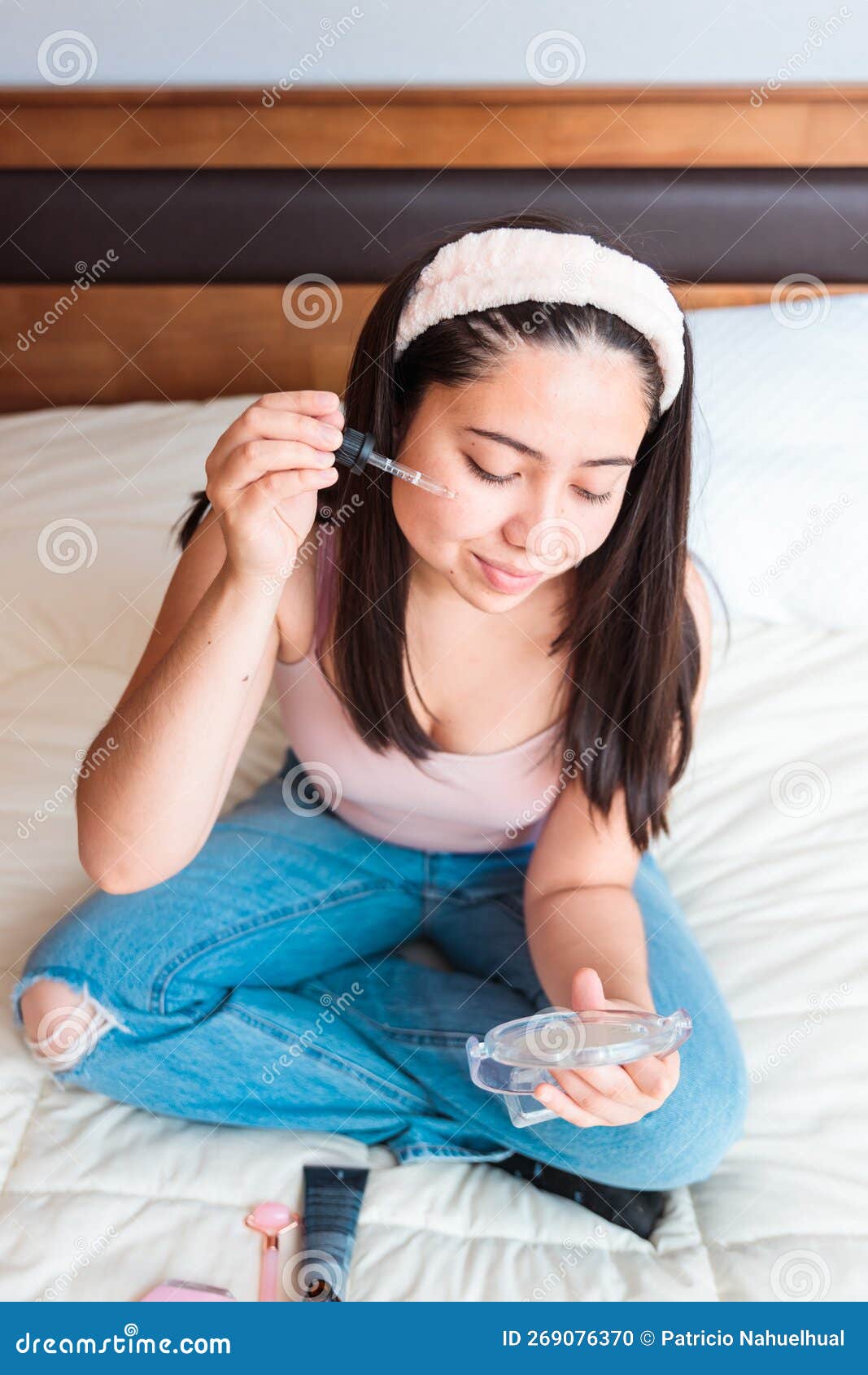 Vertical Shot Of Young Woman On Her Bed Applying Serum Collagen And