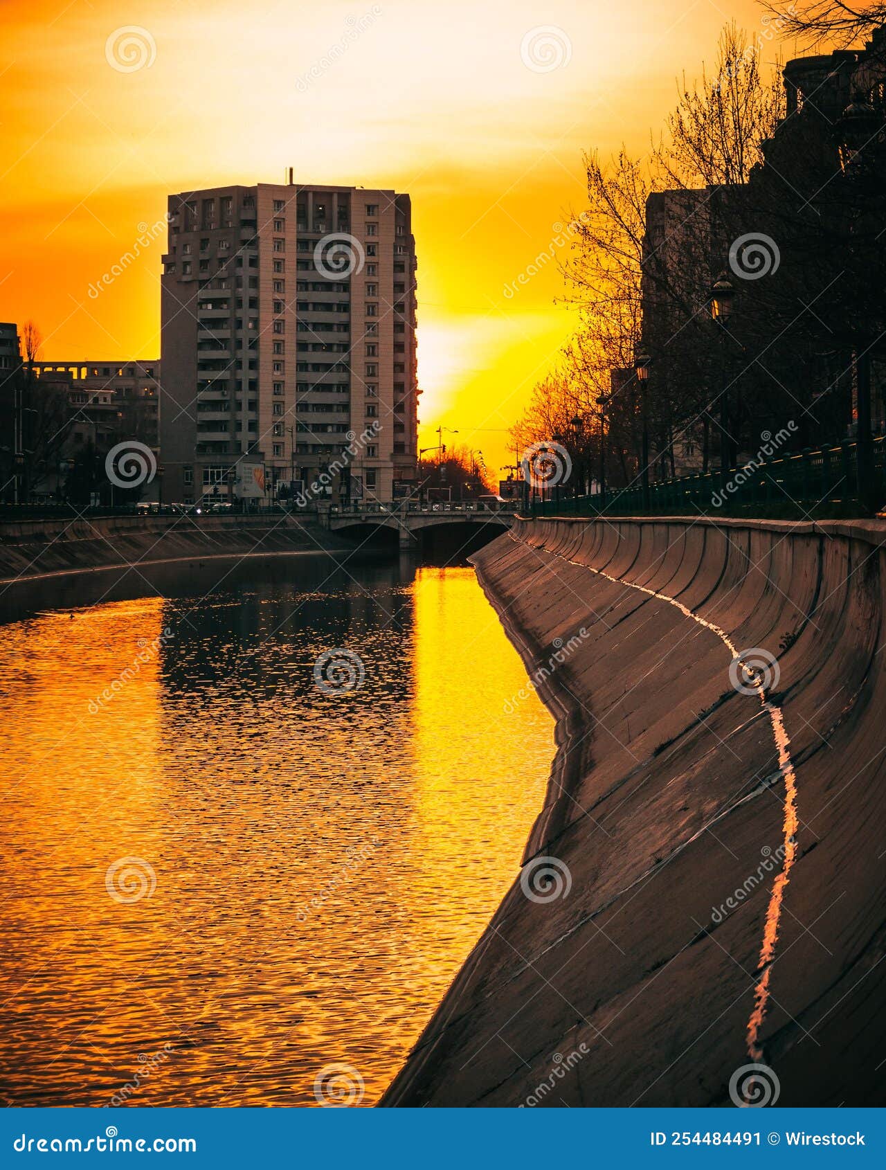 Vertical View of the Sun Setting Behind the Building on the Riverbank ...