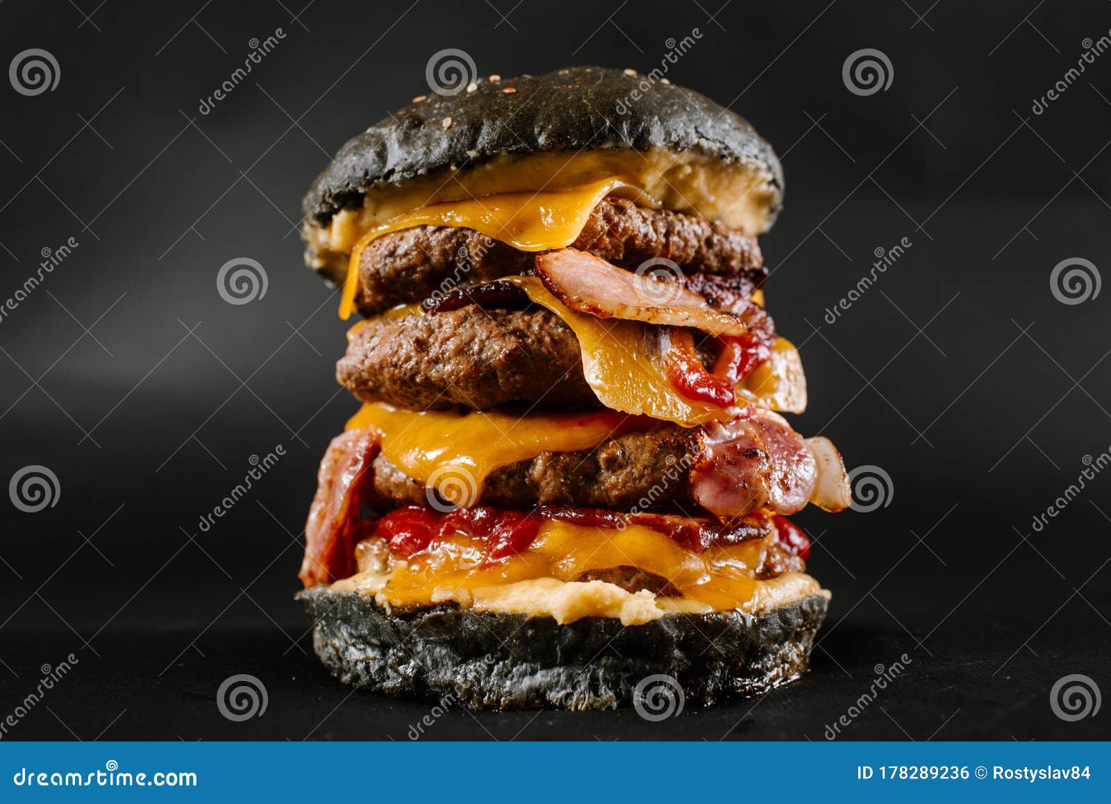 A Very Big Black Burger With Three Cutlets On The Black Background ...