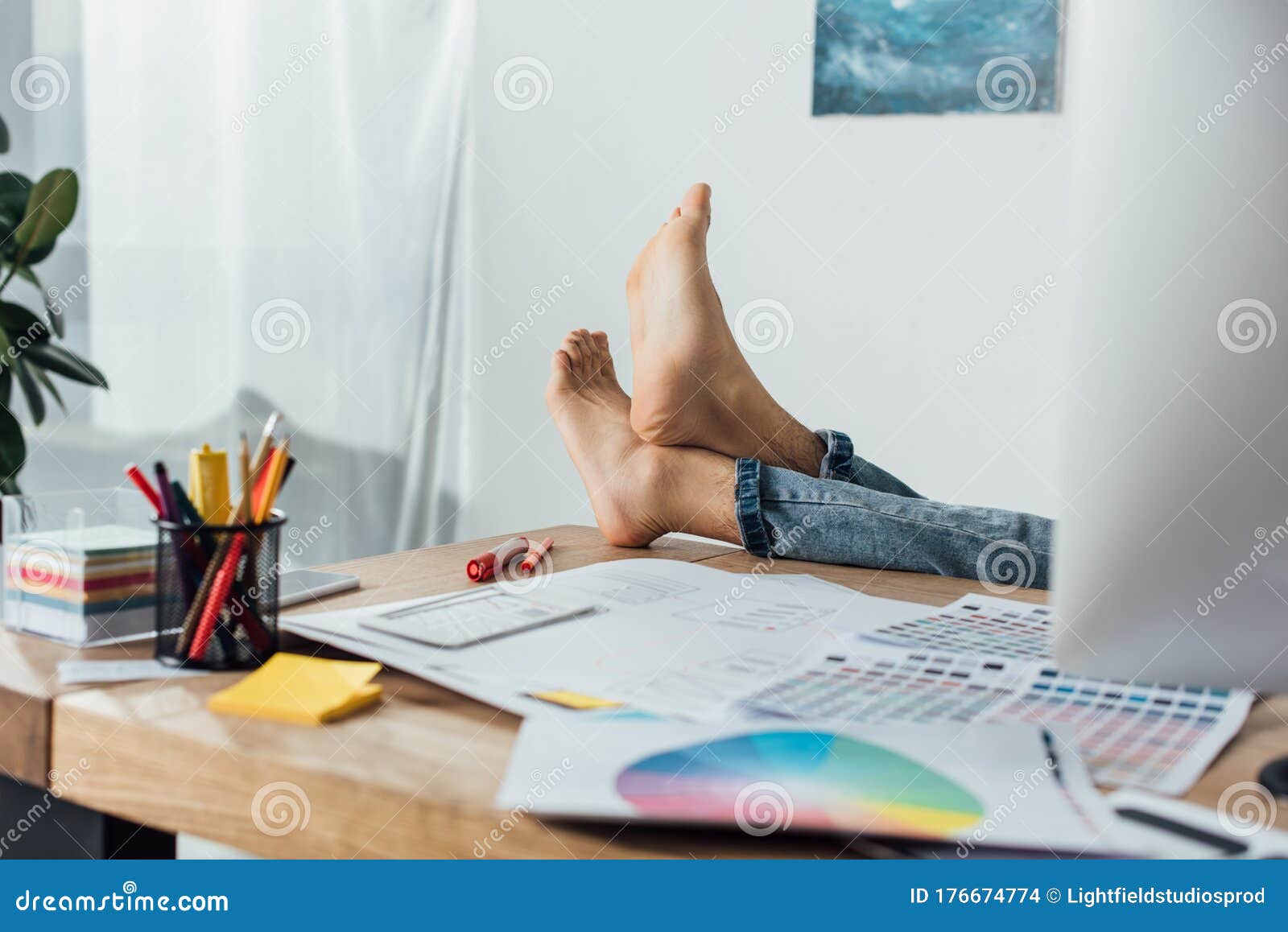 View of Barefoot Designer Sitting at Table with Computer and Layouts of ...