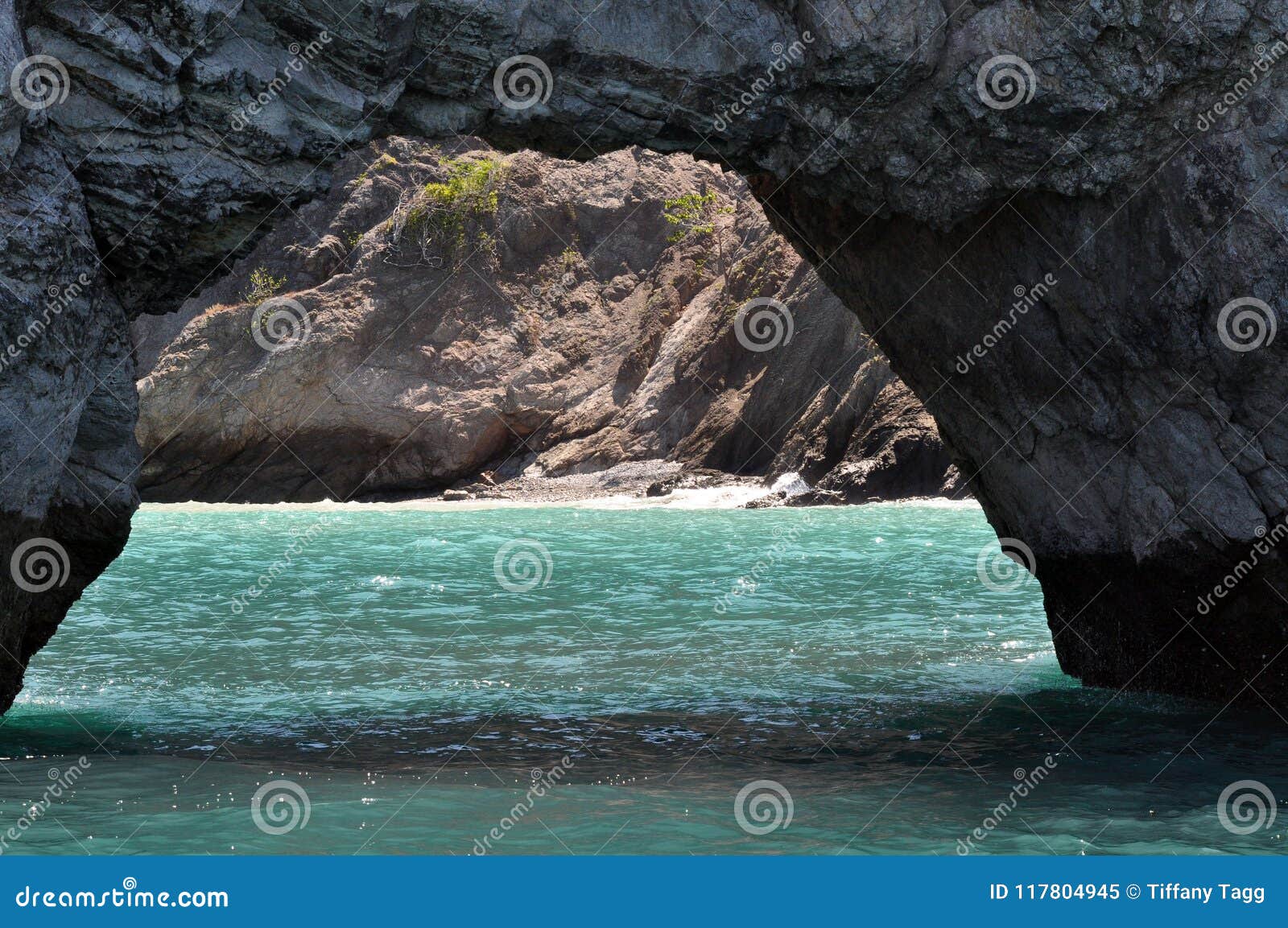 View of a Cliff through a Hole in Another Cliff with Blue Water Stock ...