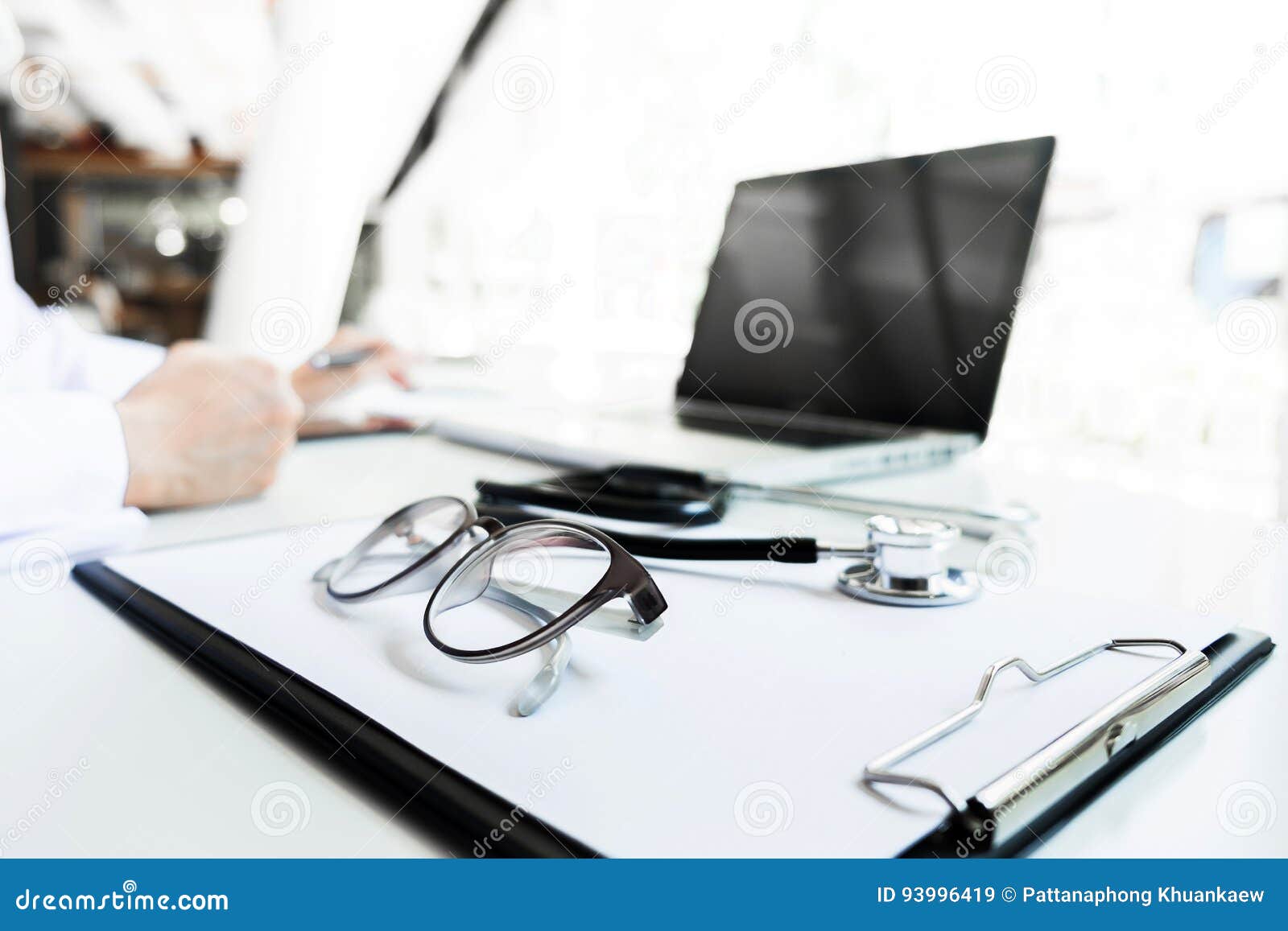View of Stethoscope and Equipment on Foreground Table with Doctor Using ...