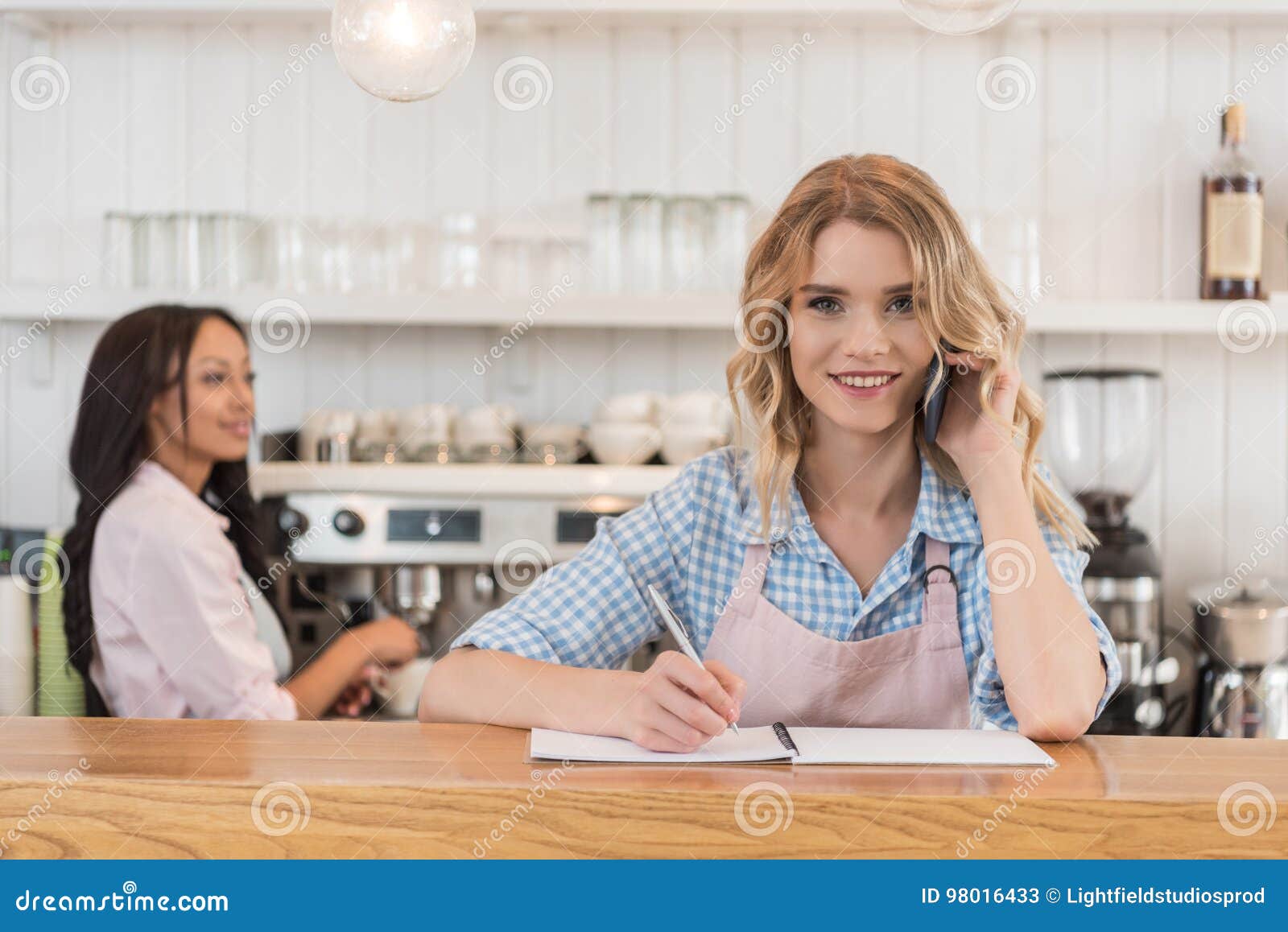 Waitress Talking on Smartphone and Making Notes in Notebook at Cafe ...