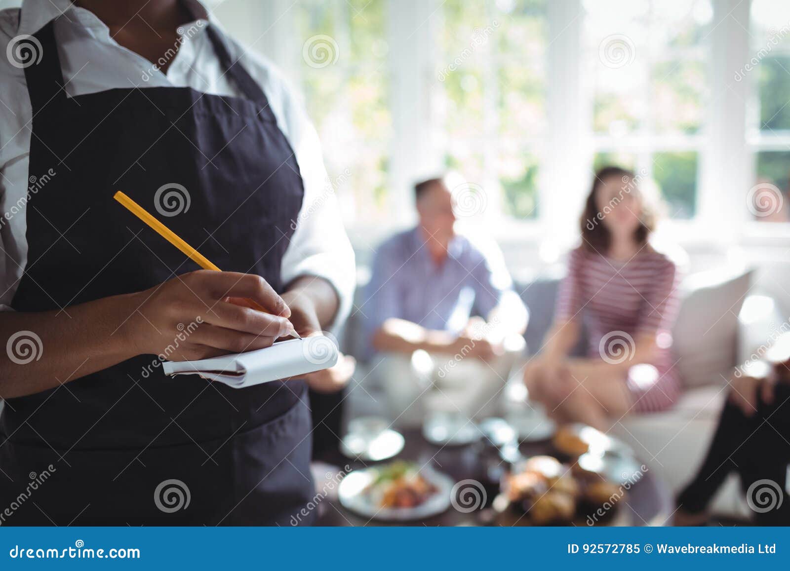 Waitress Writing on Notepad while Friends Interacting in Background ...