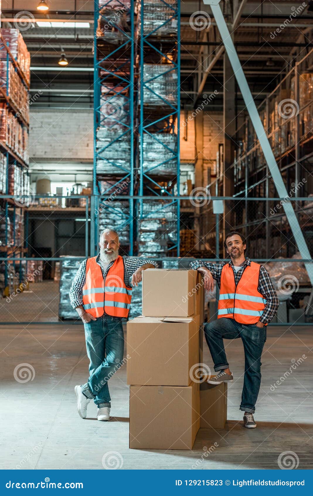 Male Warehouse Workers in Vests Standing with Boxes and Smiling Stock ...