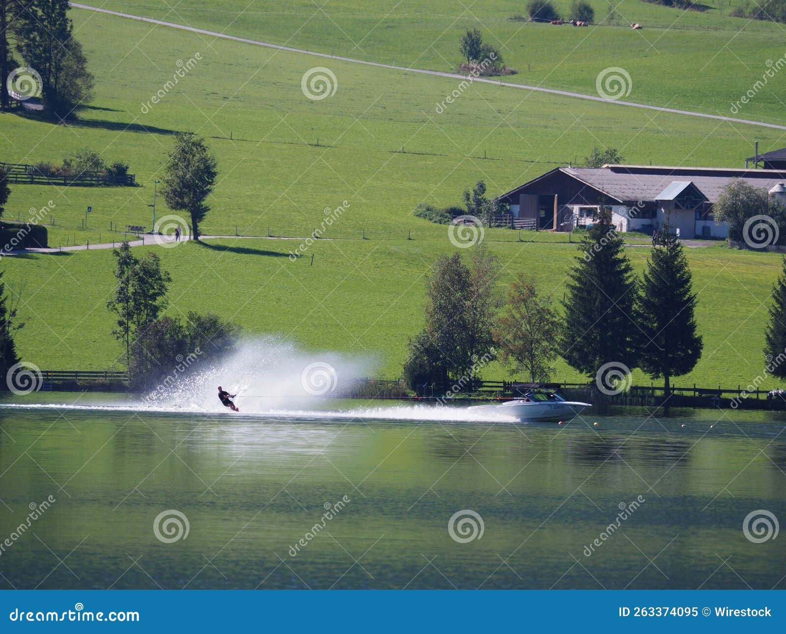 Water Skier with a Boat in Front of an Alpine Farm Backdrop with a Barn ...