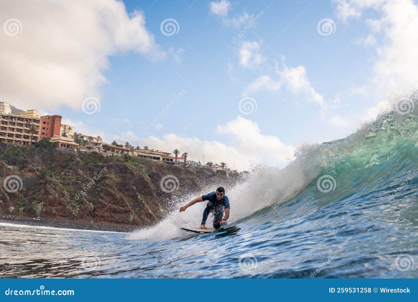 White Man Riding a Beach Wave with Buildings and Clouds in the ...