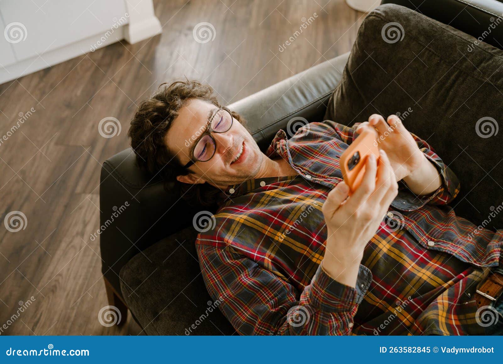 White Man Smiling and Using Mobile Phone while Resting on Couch Stock ...