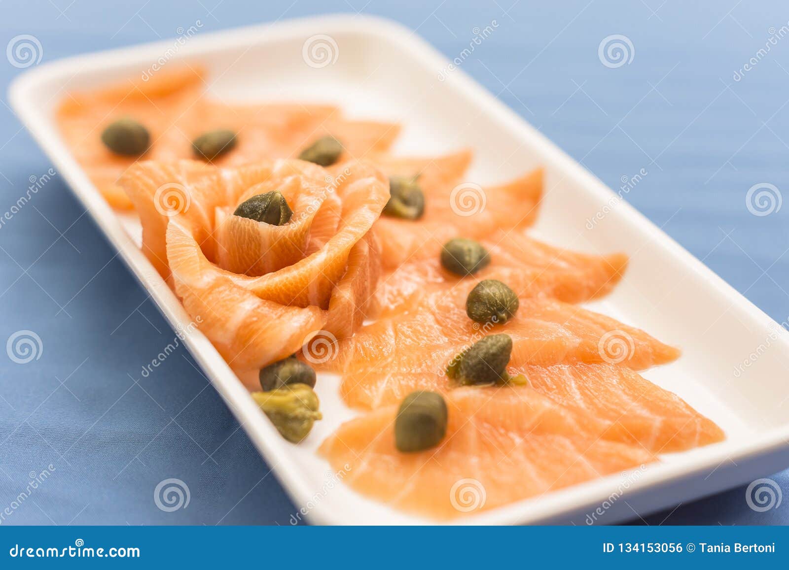 White Plate with Salmon Sashimi and Capers on Blue Background Stock ...
