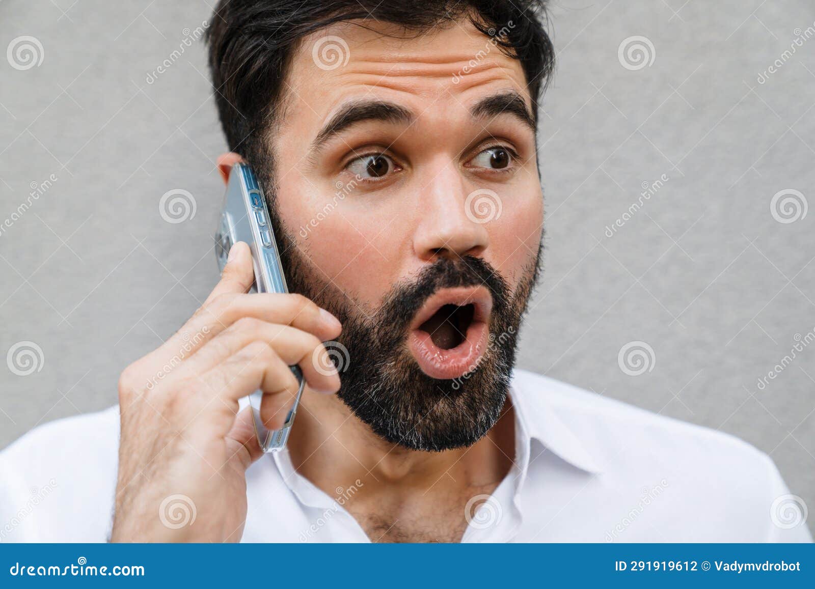 White Shocked Man Talking On Mobile Phone While Standing By Wall Stock