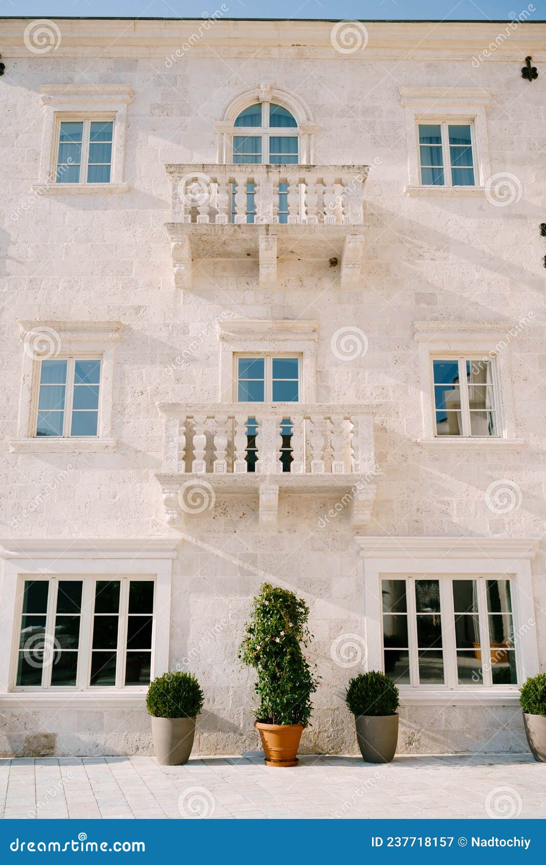 White Stone Building Facade with Balconies and Flowerpots on a Tiled ...