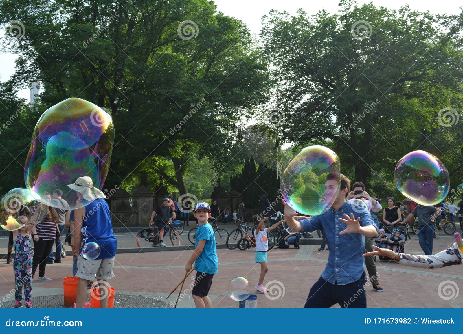 Wide Angle Shot of People Blowing Bubbles on the Street Behind Trees ...