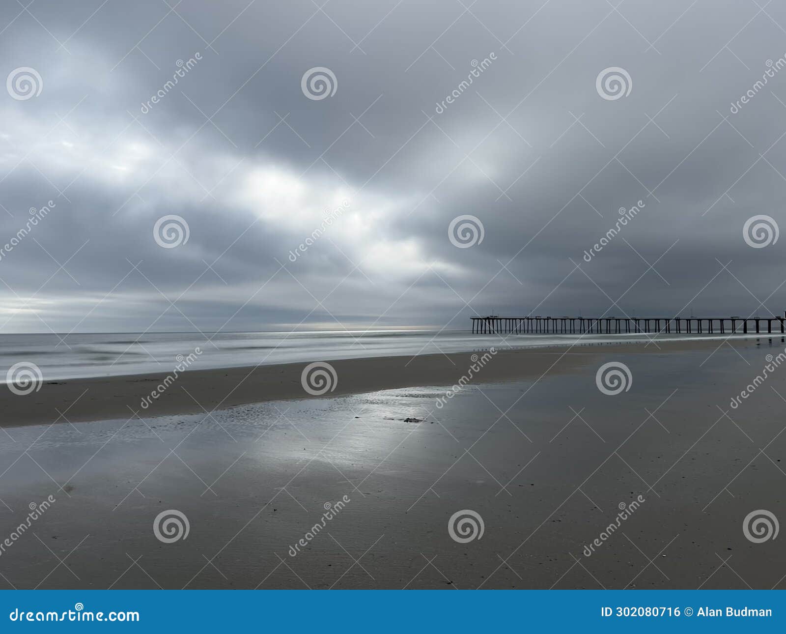Wide Wet Desolate Beach with Storm Clouds and a Long Pier Going Out ...
