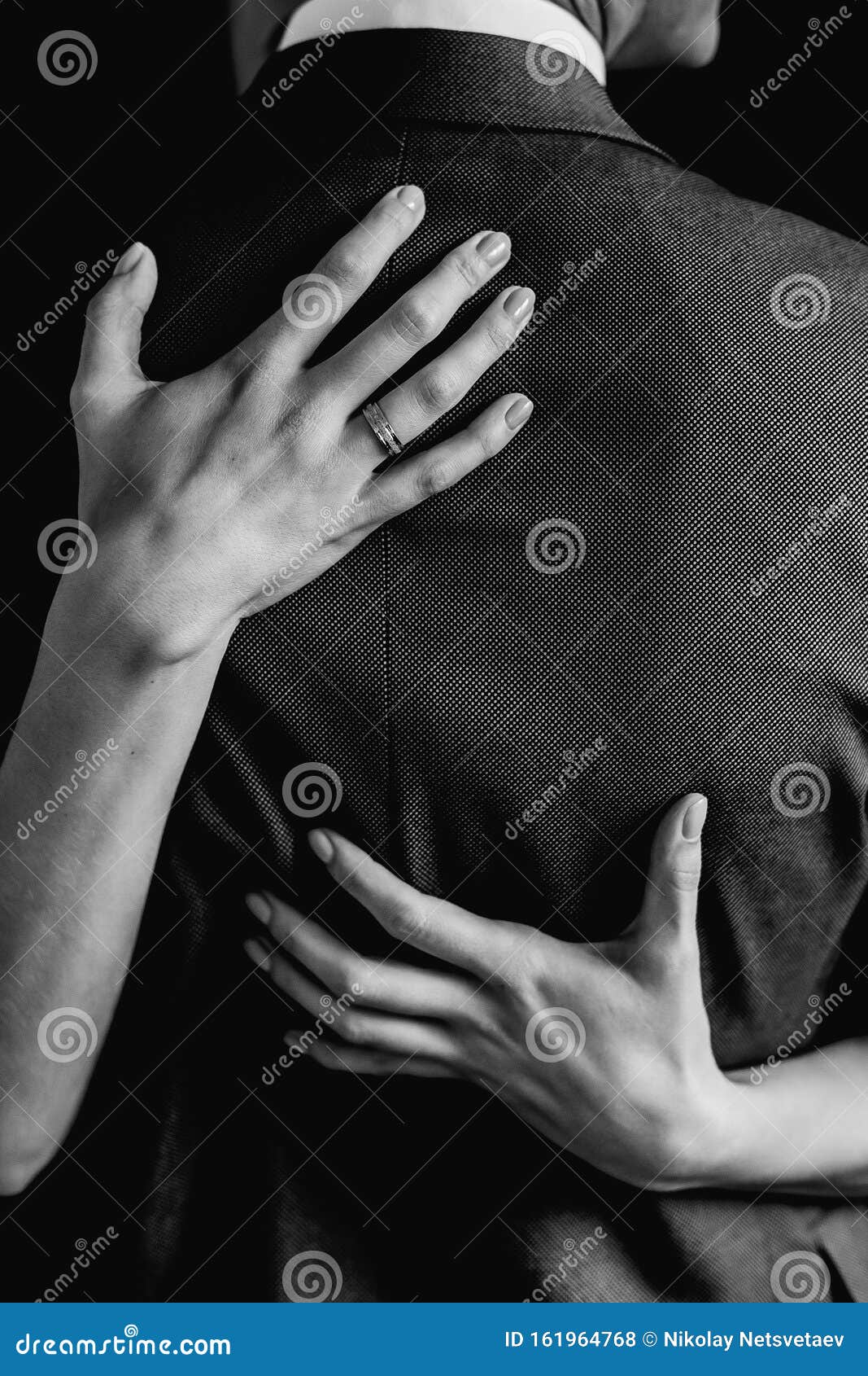 Bride Hugs The Groom In A Jacket With Two Hands In Black And White