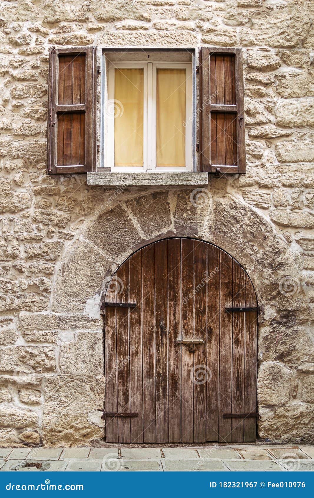 A Window with Open Shutters Over a Closed Gate in an Old Stone Wall ...