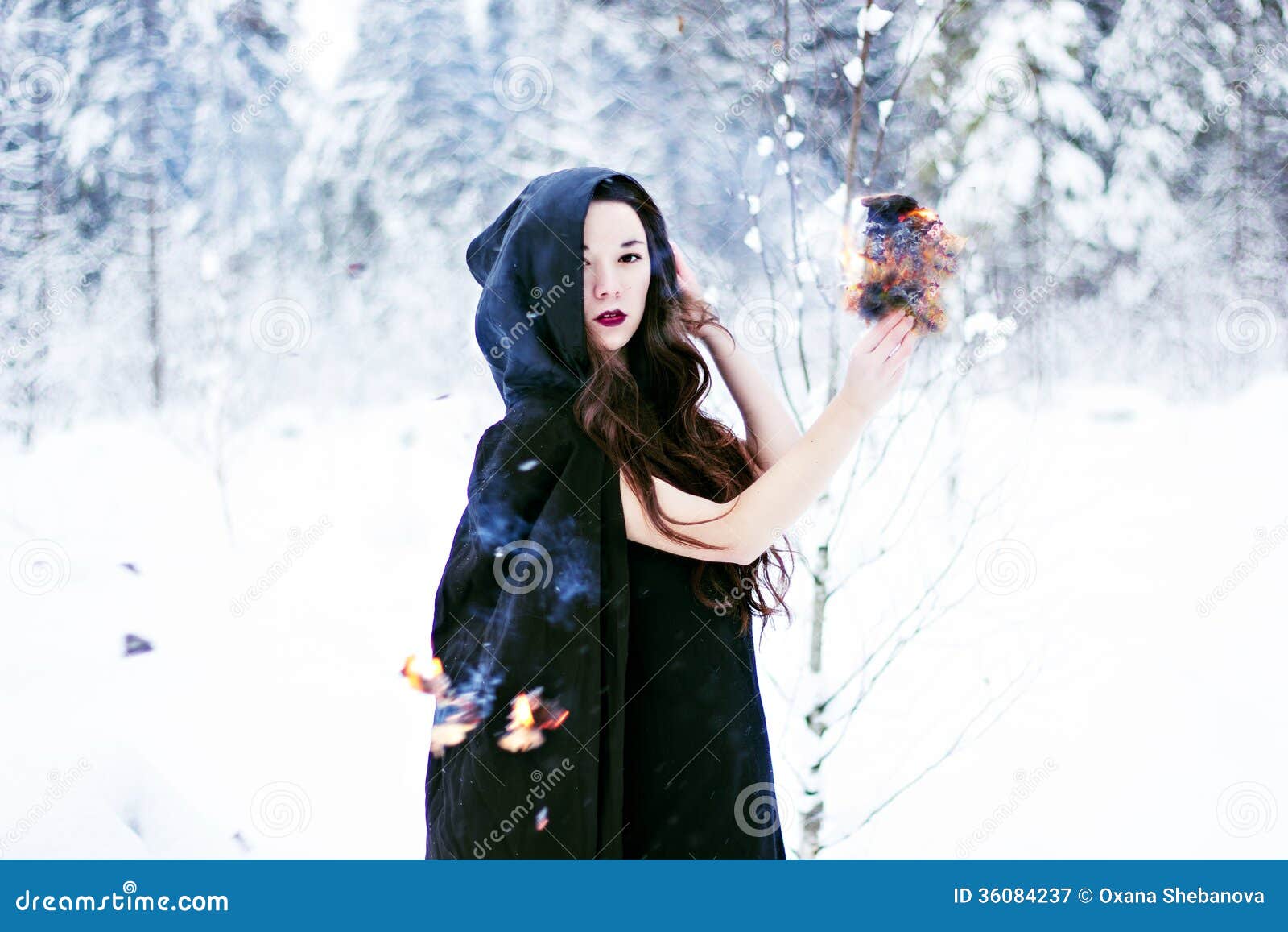 Witch or Woman in Black Cloak with Fire Ball in White Snow Forest Stock ...