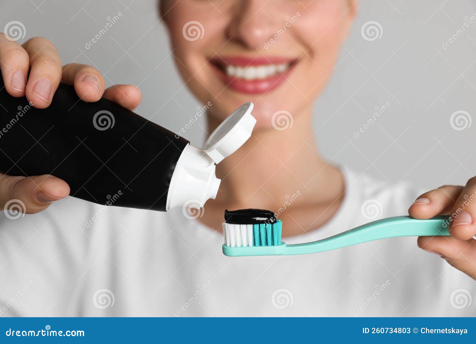 Woman Applying Charcoal Toothpaste Onto Brush On Grey Background