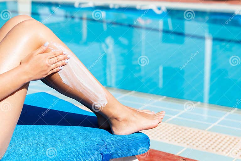 Woman Is Applying Sunscreen On Her Tanned Legs By The Swimming Pool