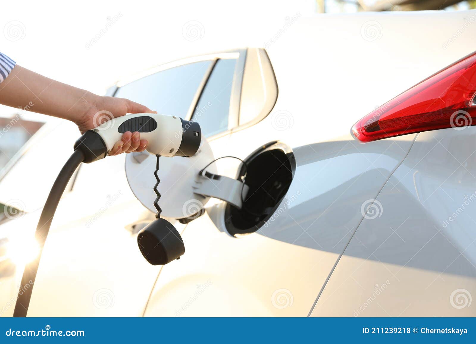 Woman Inserting Plug into Electric Car Socket at Charging Station ...