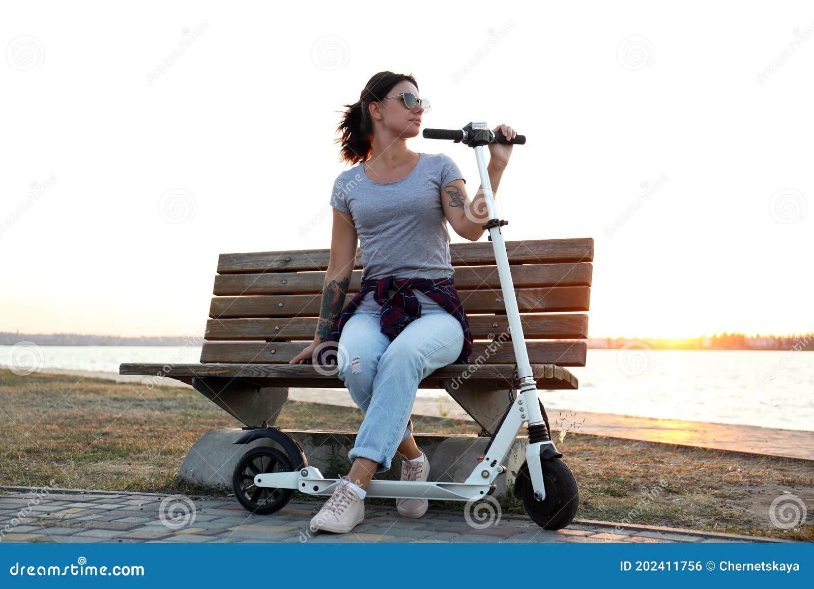 Young Woman with Kick Scooter Sitting on Bench Outdoors Stock Photo ...