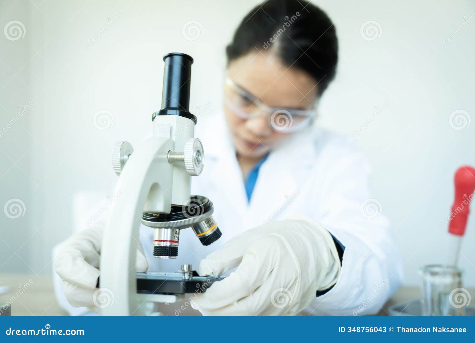 A Woman in a Lab Coat is Looking through a Microscope. she is Wearing ...