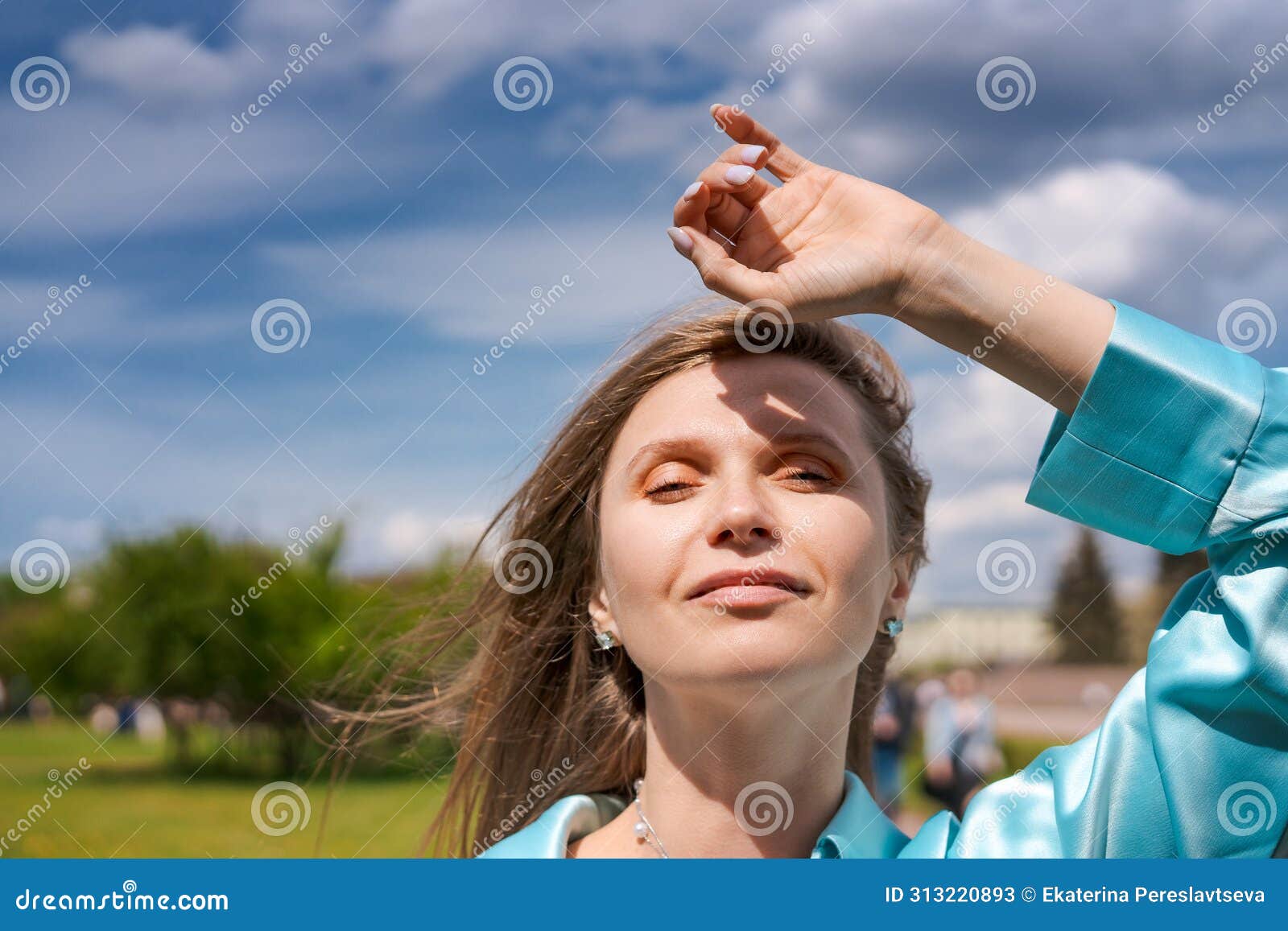 A Woman With Long Blonde Hair Is Standing In A Park Looking Up At Sky