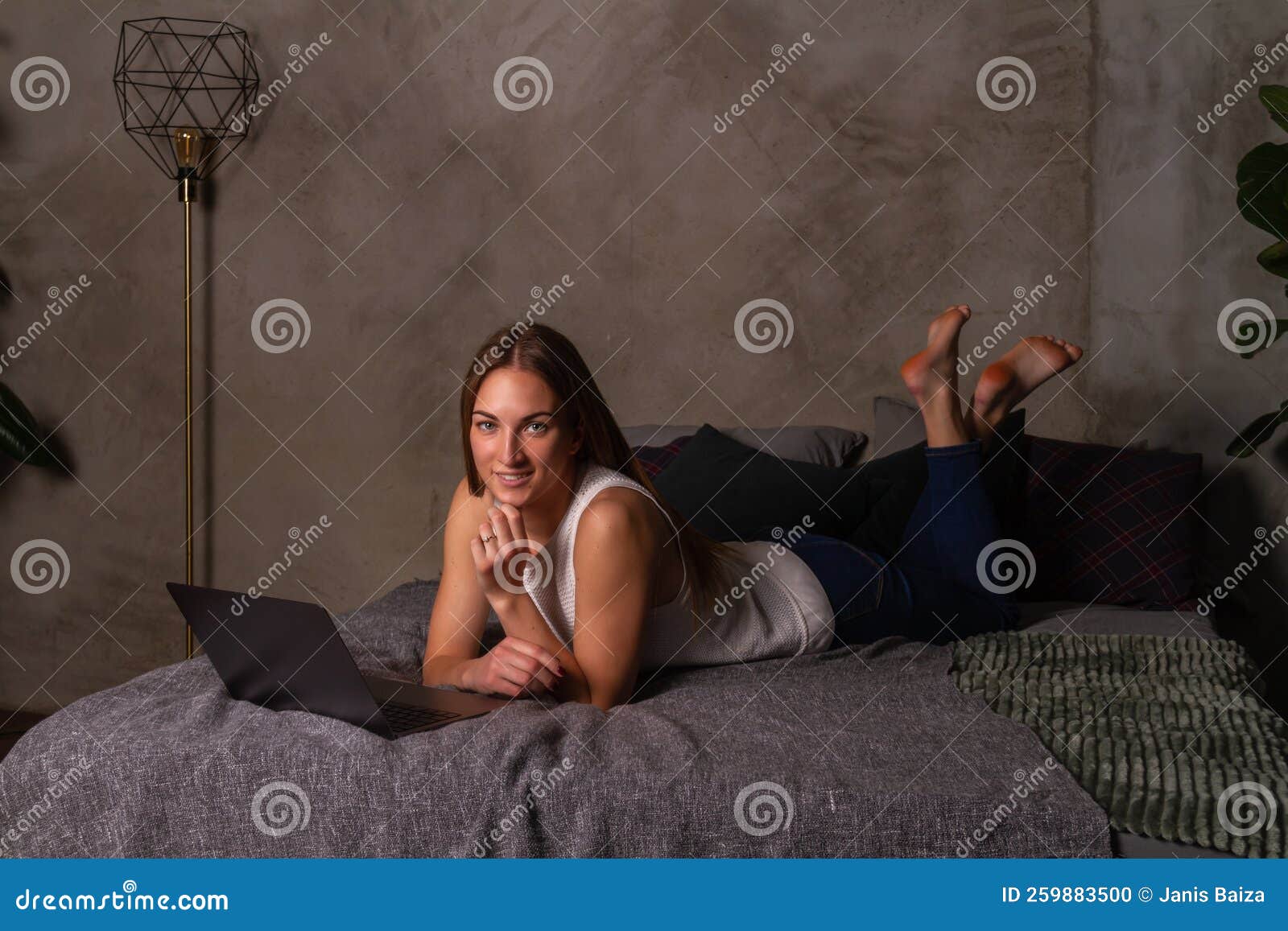 Woman Lying On Her Stomach In Bed With Laptop In Front Of Her Stock