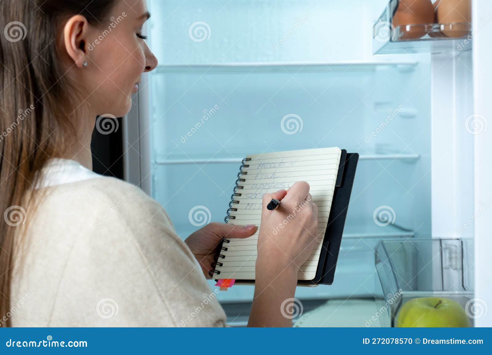 Woman Makes a Shopping List in a Notebook, Standing by an Empty ...
