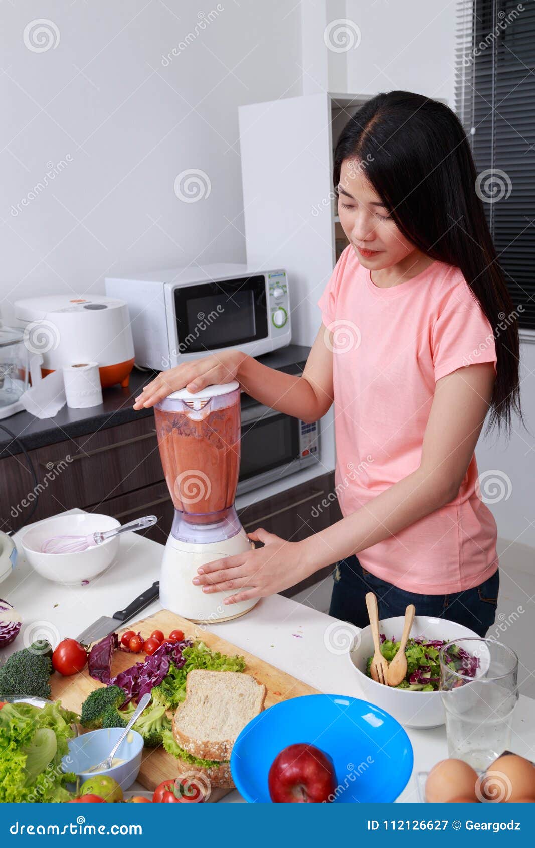 Woman Making Vegetable Smoothies With Blender In Kitchen Stock Image