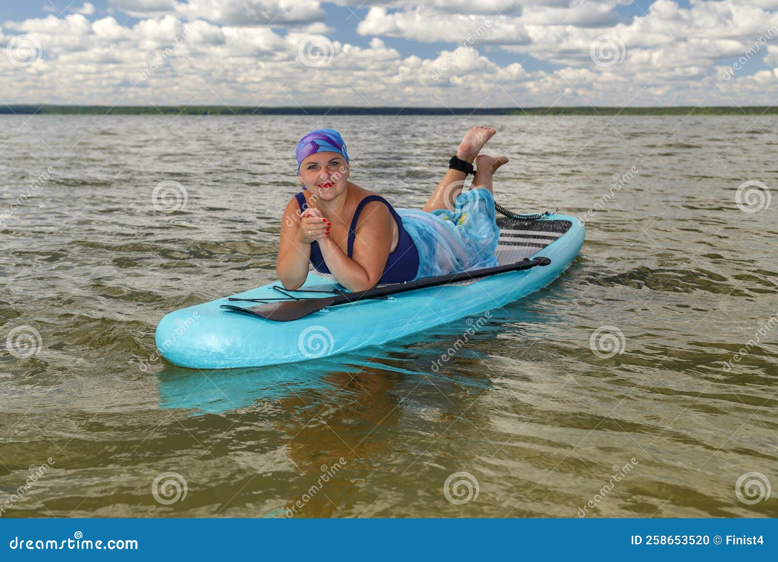 A Woman With A Mohawk In A Pareo Is Sunbathing On A Sup Board In A Lake