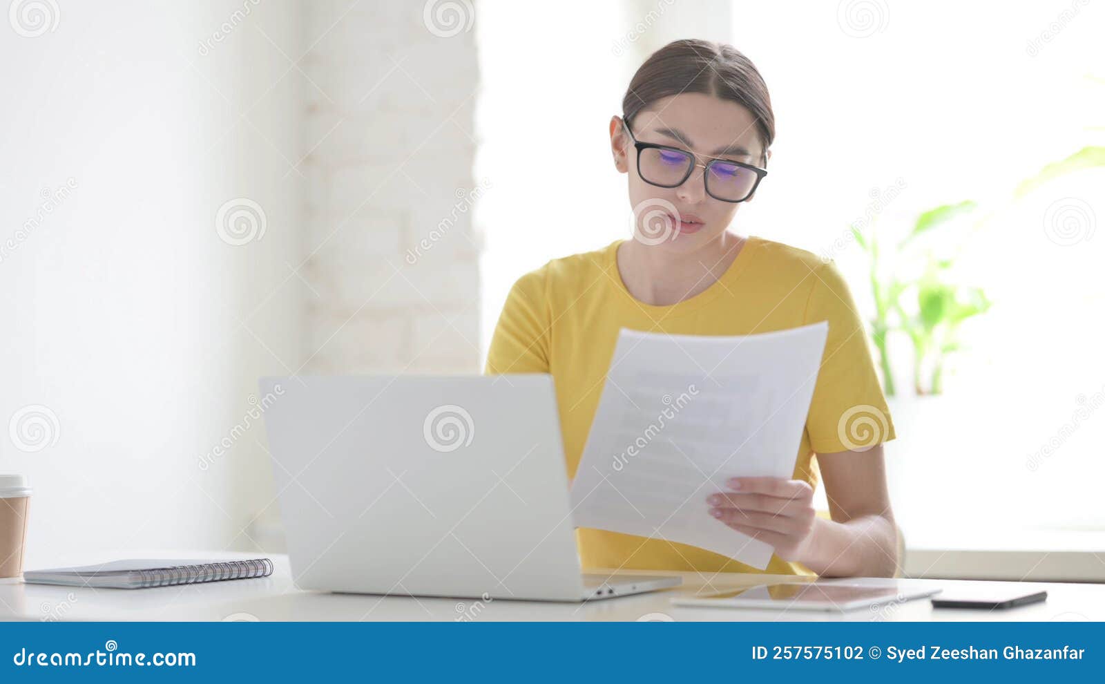 Woman Reading Documents while Using Laptop in Office Stock Photo ...