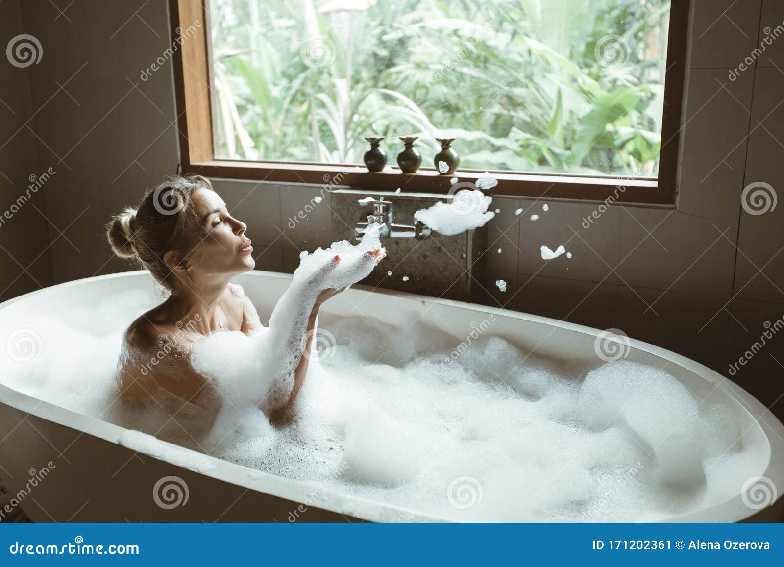 Woman Relaxing In Foam Bath With Bubbles In Dark Bathroom By Window