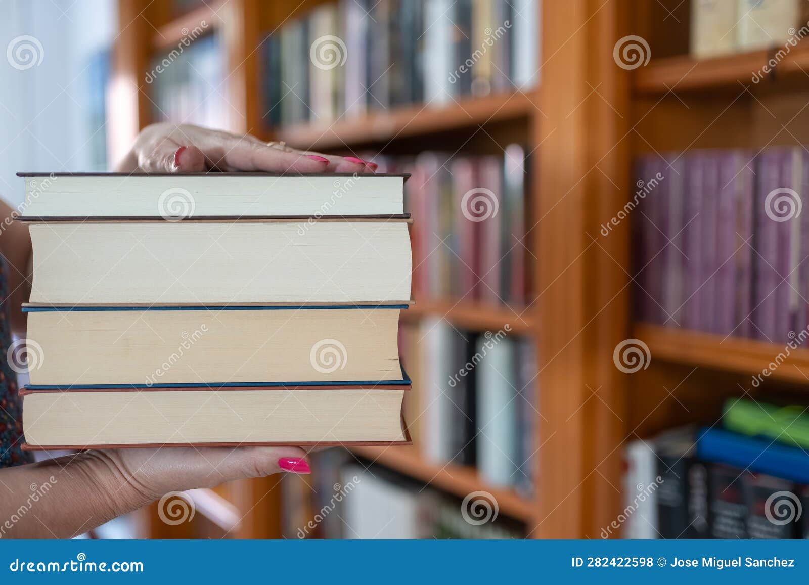 Woman S Hands Holding a Stack of Books in Front of a Bookstore Full of ...