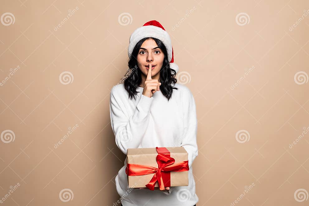 Young Woman in Santa Claus Dress with Gift Box Showing Silence Gesture ... Young Woman in Santa Claus Dress with Gift Box Showing Silence Gesture ...
